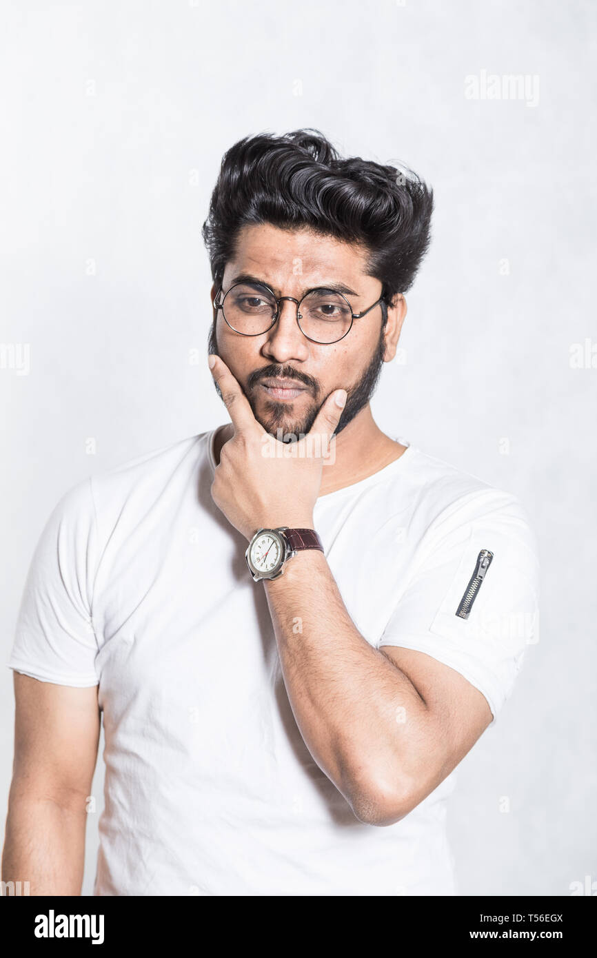 Embarrassed unsure man with glasses holds his chin and purses his lips ...