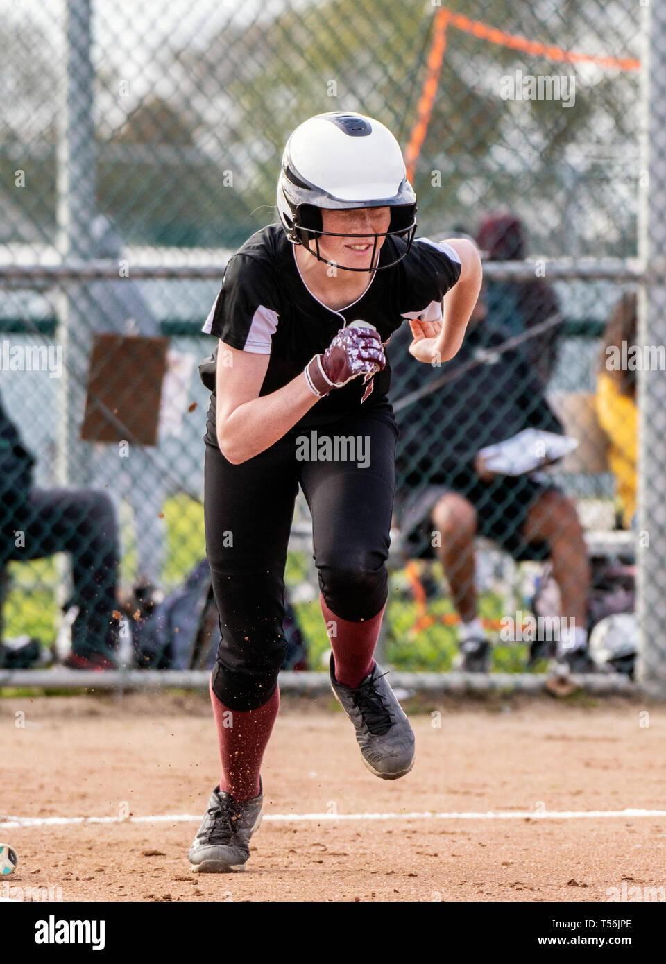 Female softball base runner smiling through her face mask while ...