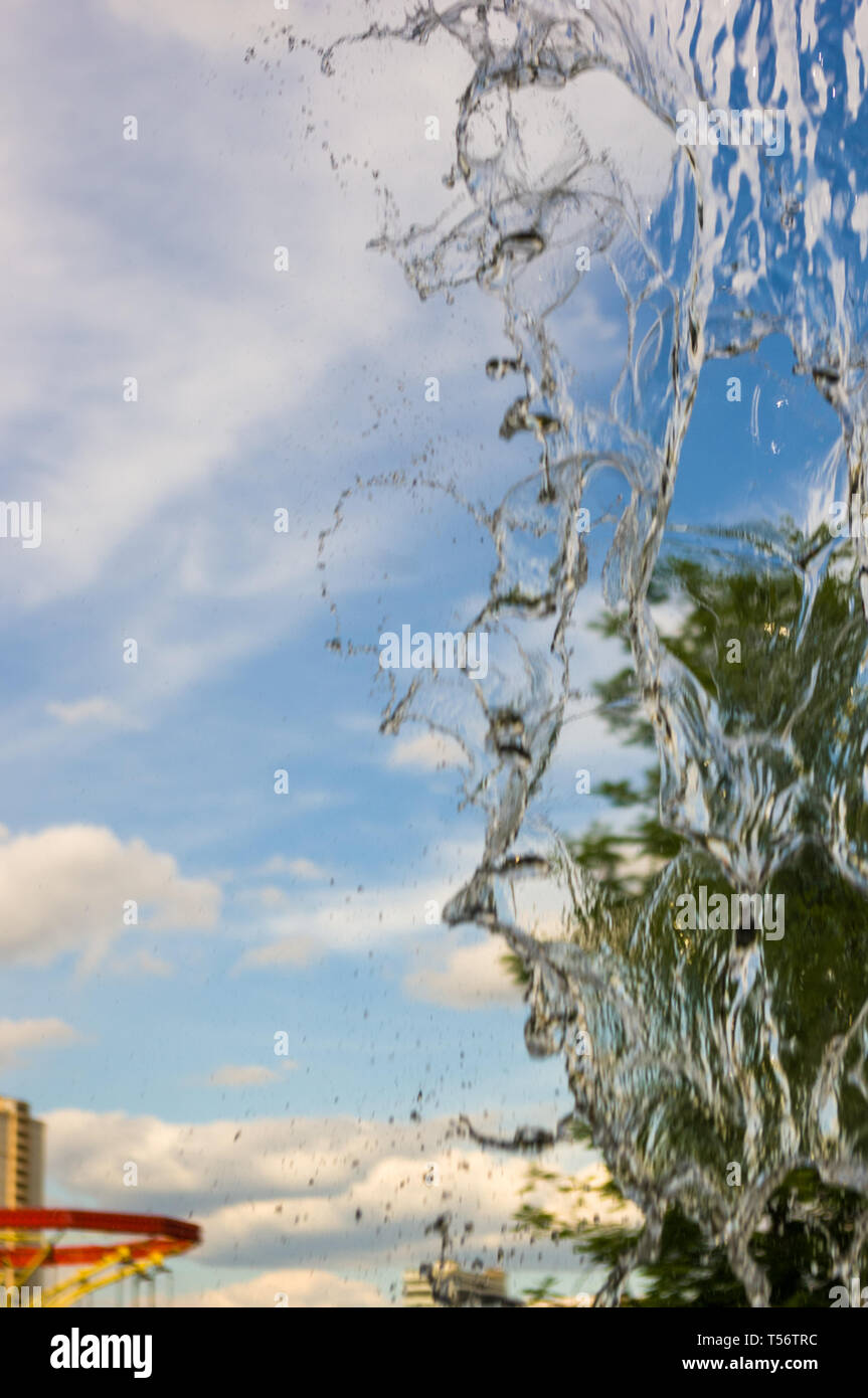 transparent falling water vertical flows against a blue sky and green ...
