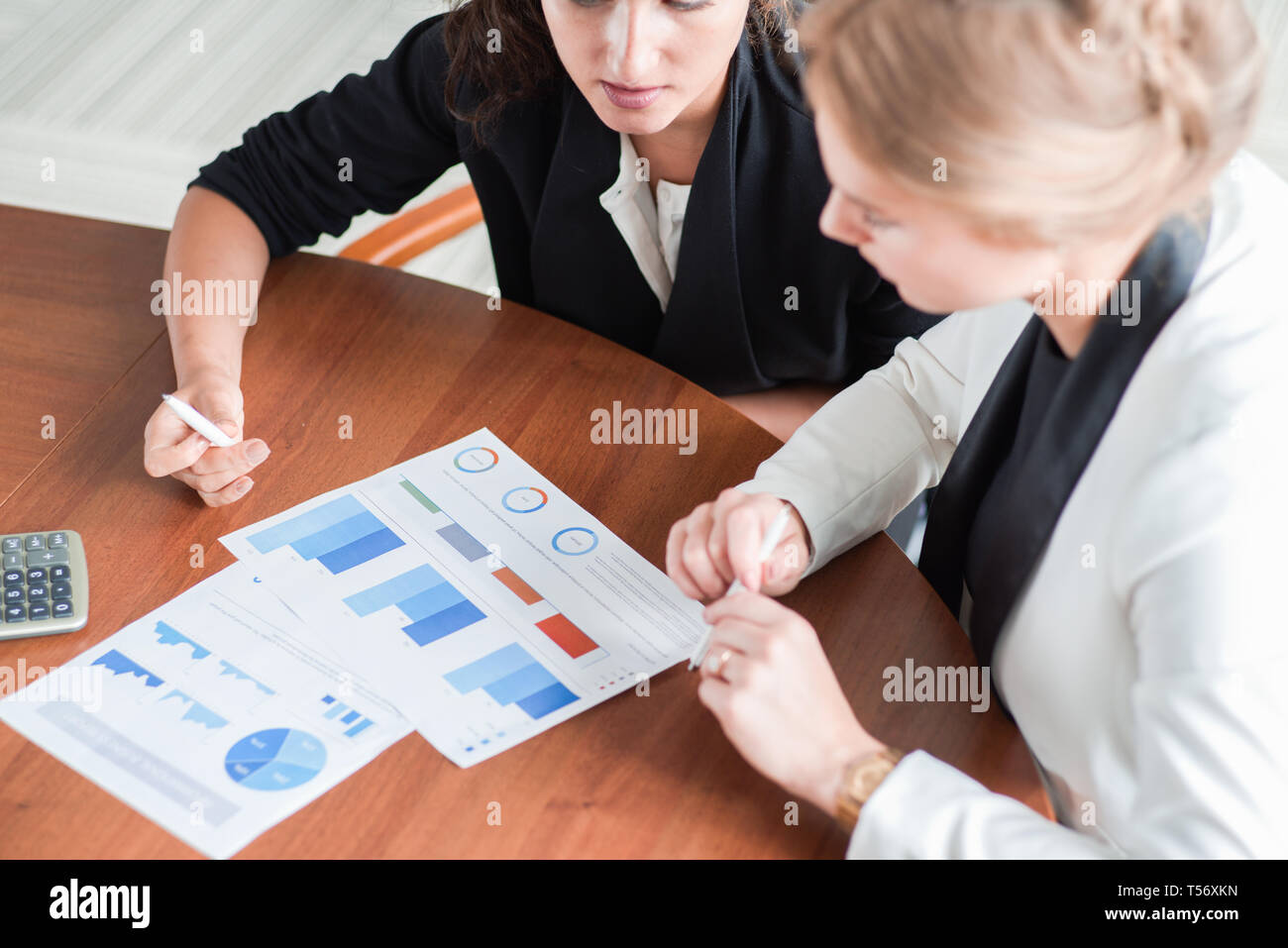 Business women pointing at diagrams discussing financial reports at ...