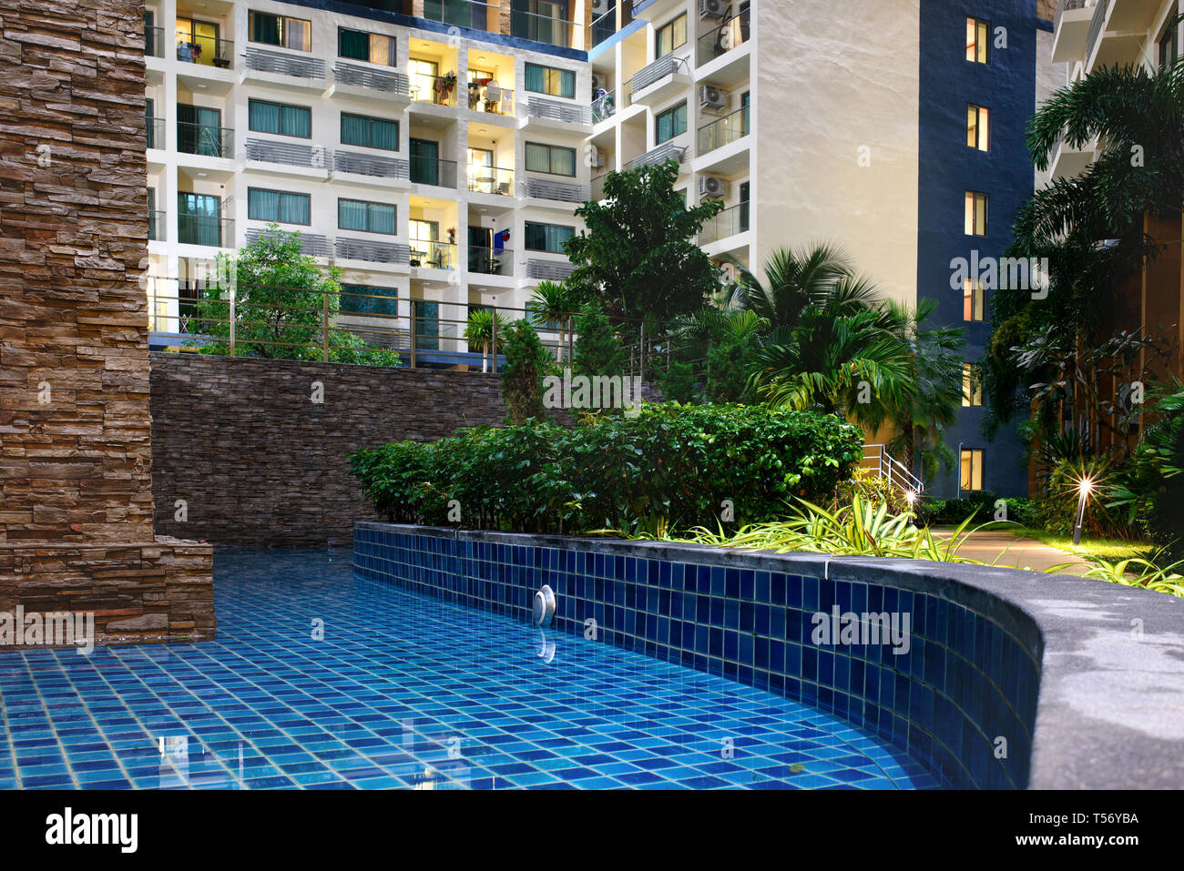 Iluminated swimming pool and palm trees between buildings at night ...
