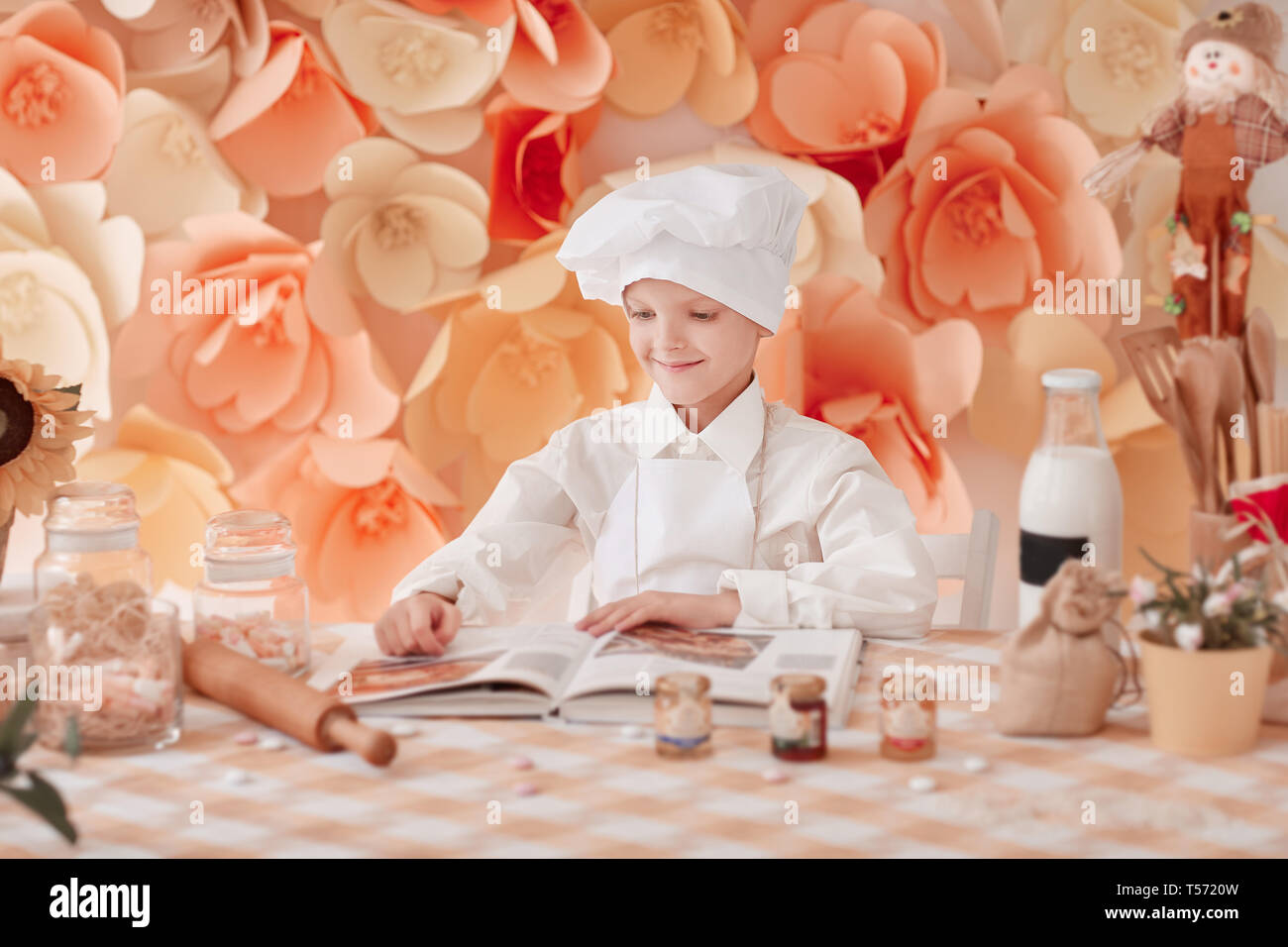 happy boy in a chef's uniform is reading a cookbook. the concept of a ...