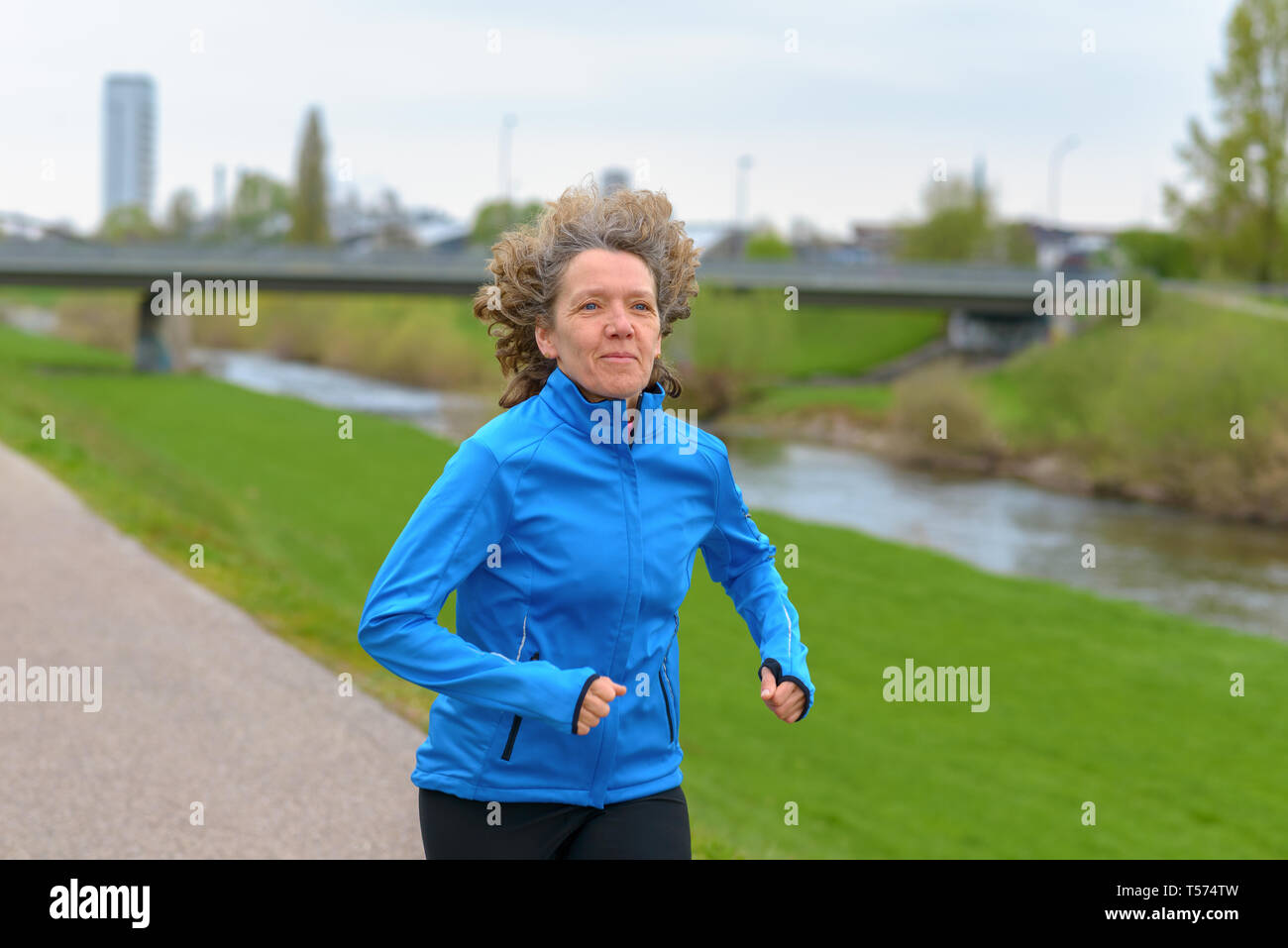 Fit athletic middle-aged woman jogging on a road alongside a canal ...