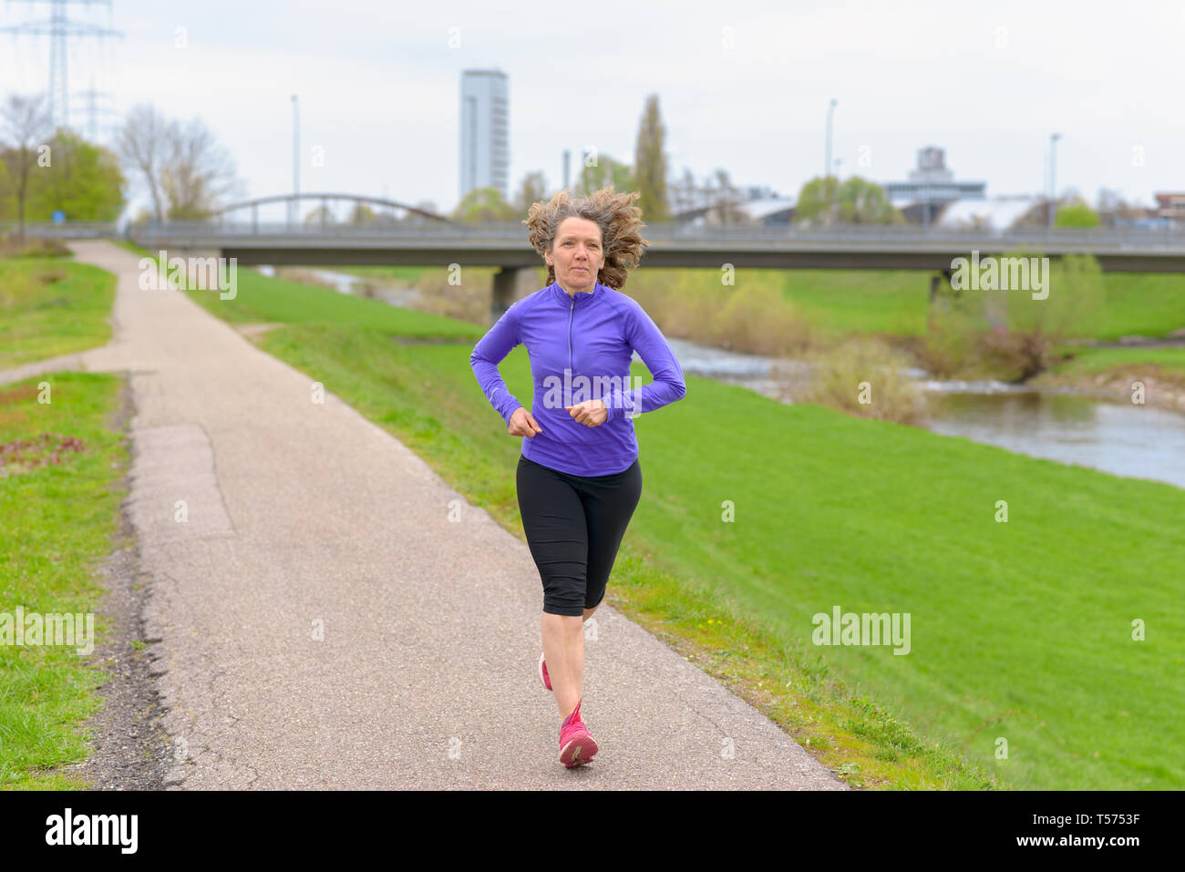 Athletic woman jogging alongside a river on a grey cloudy day ...