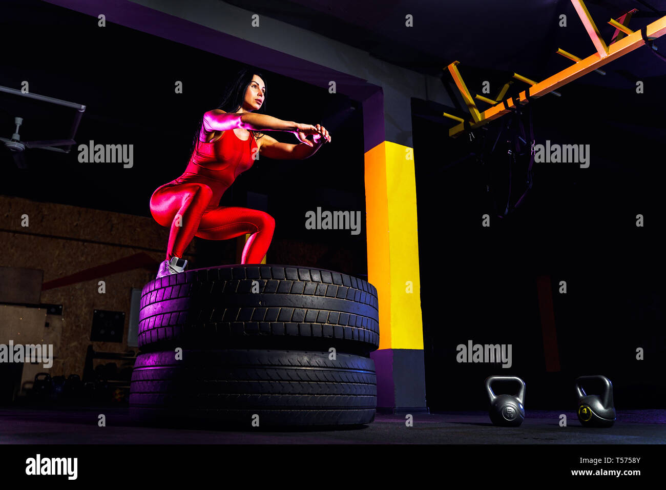 Fit young woman jumping on tire at gym. Female athlete is performing ...