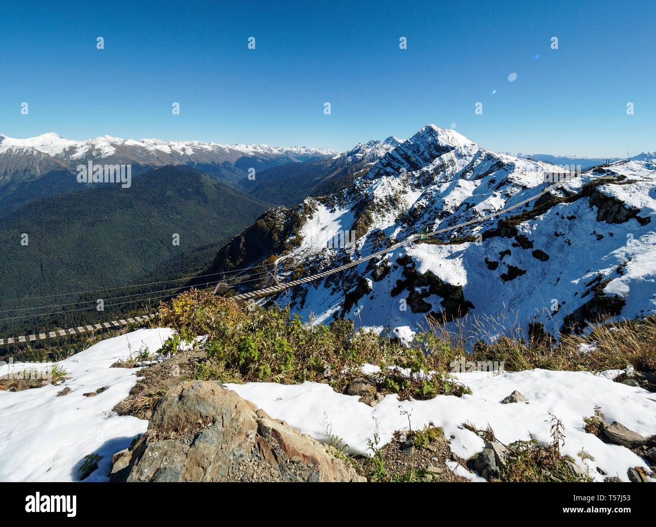Suspended pedestrian bridge in the high snowy mountains. Clear blue sky ...