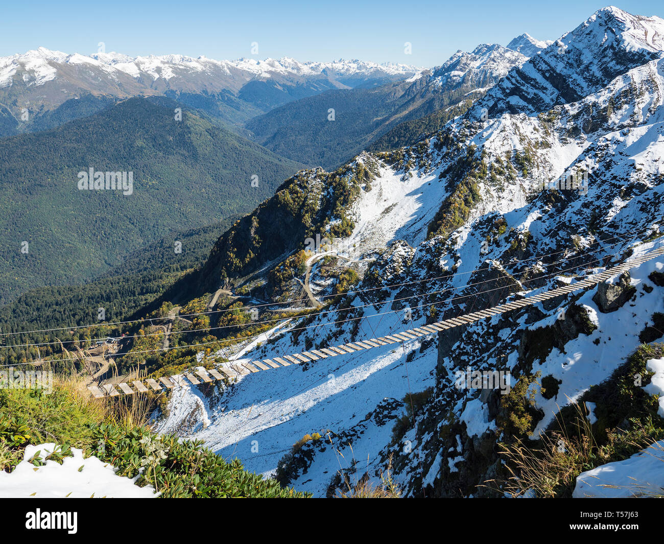 Suspended pedestrian bridge in the high snowy mountains. Clear blue sky ...