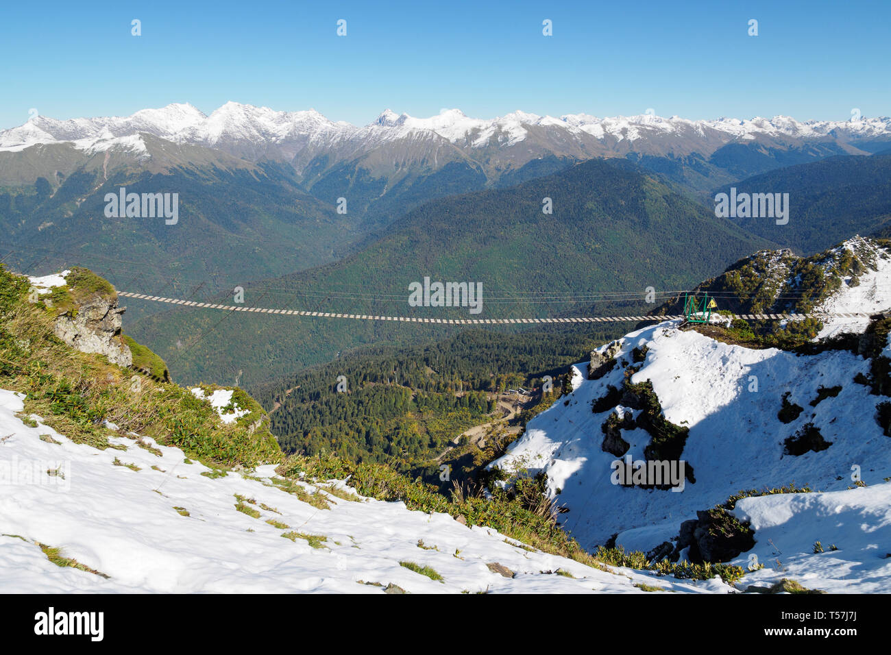 Suspended pedestrian bridge in the high snowy mountains. Clear blue sky ...