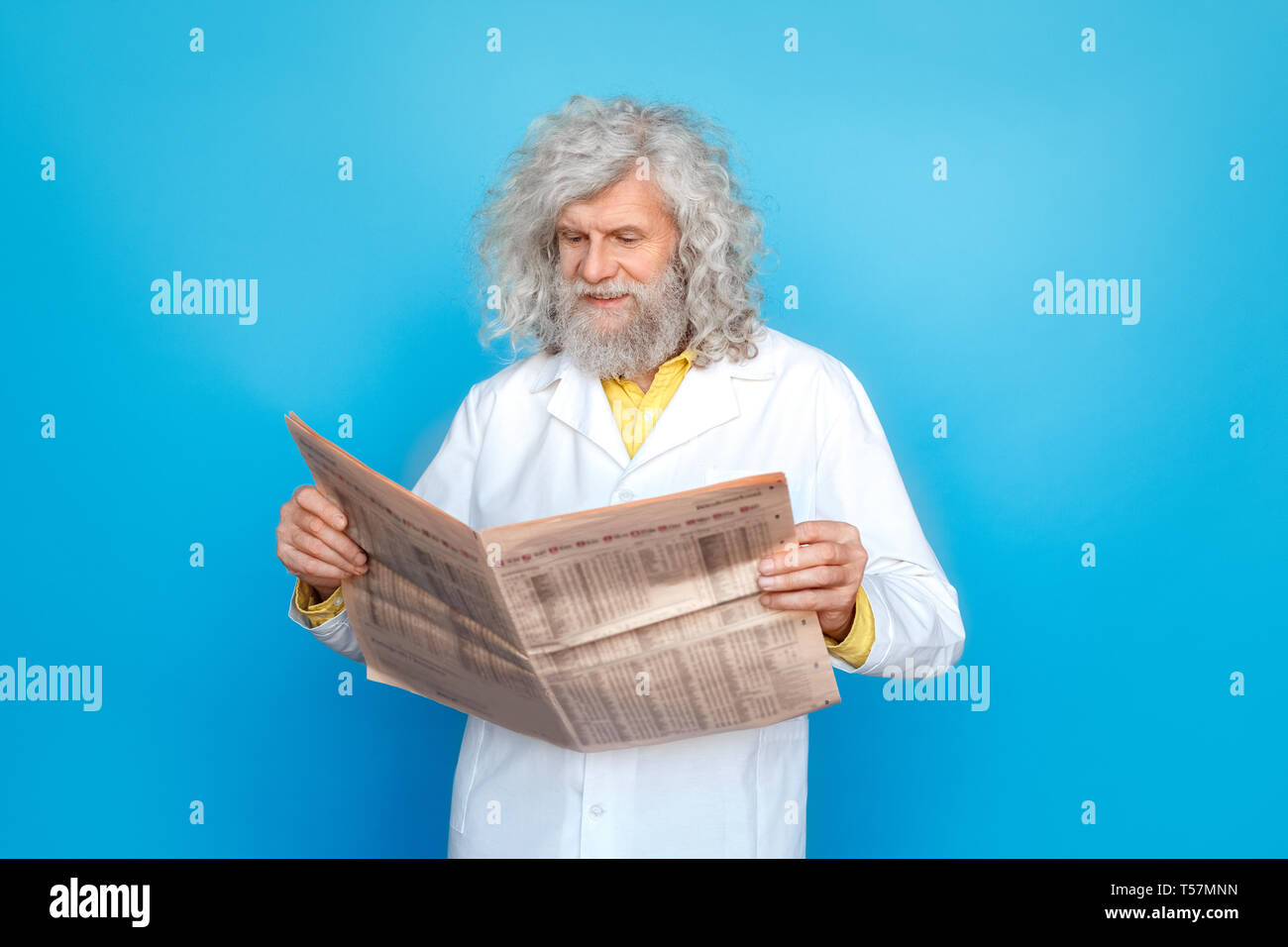 Old long-haired man wearing doctor's gown studio isolated on blue wall ...