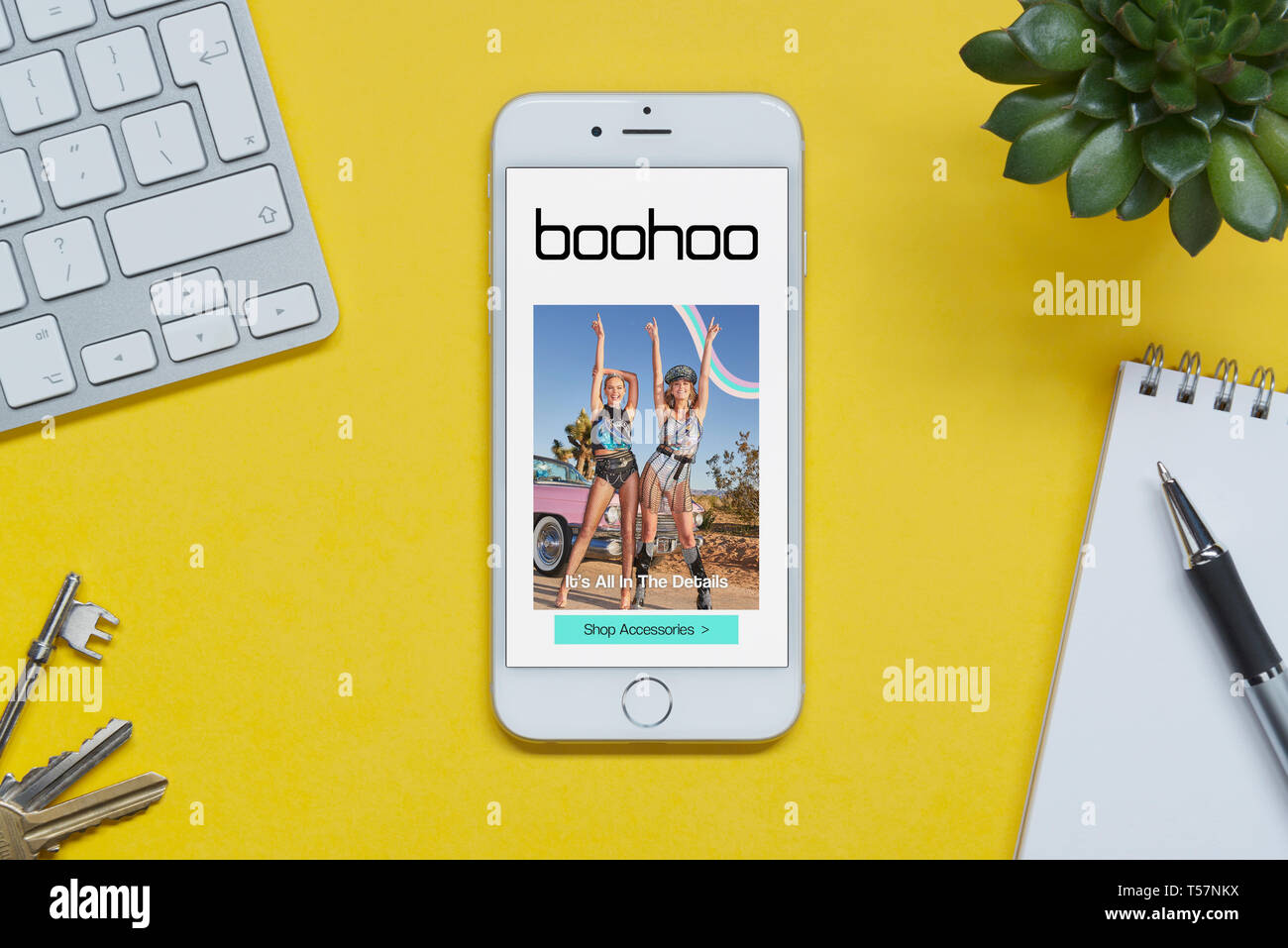 An iPhone showing the Boohoo website rests on a yellow background table ...