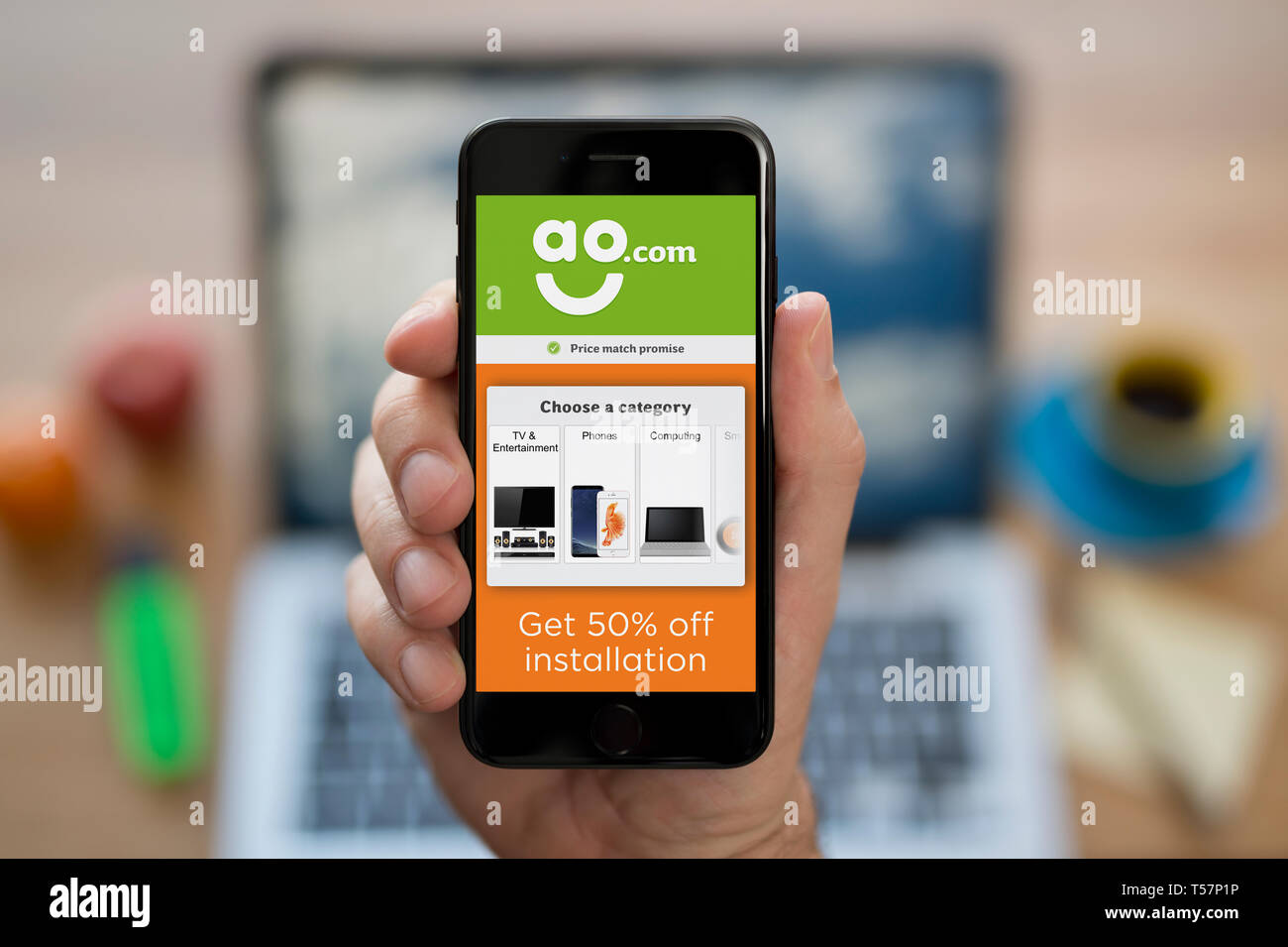 A man looks at his iPhone which displays the ao.com logo (Editorial use ...