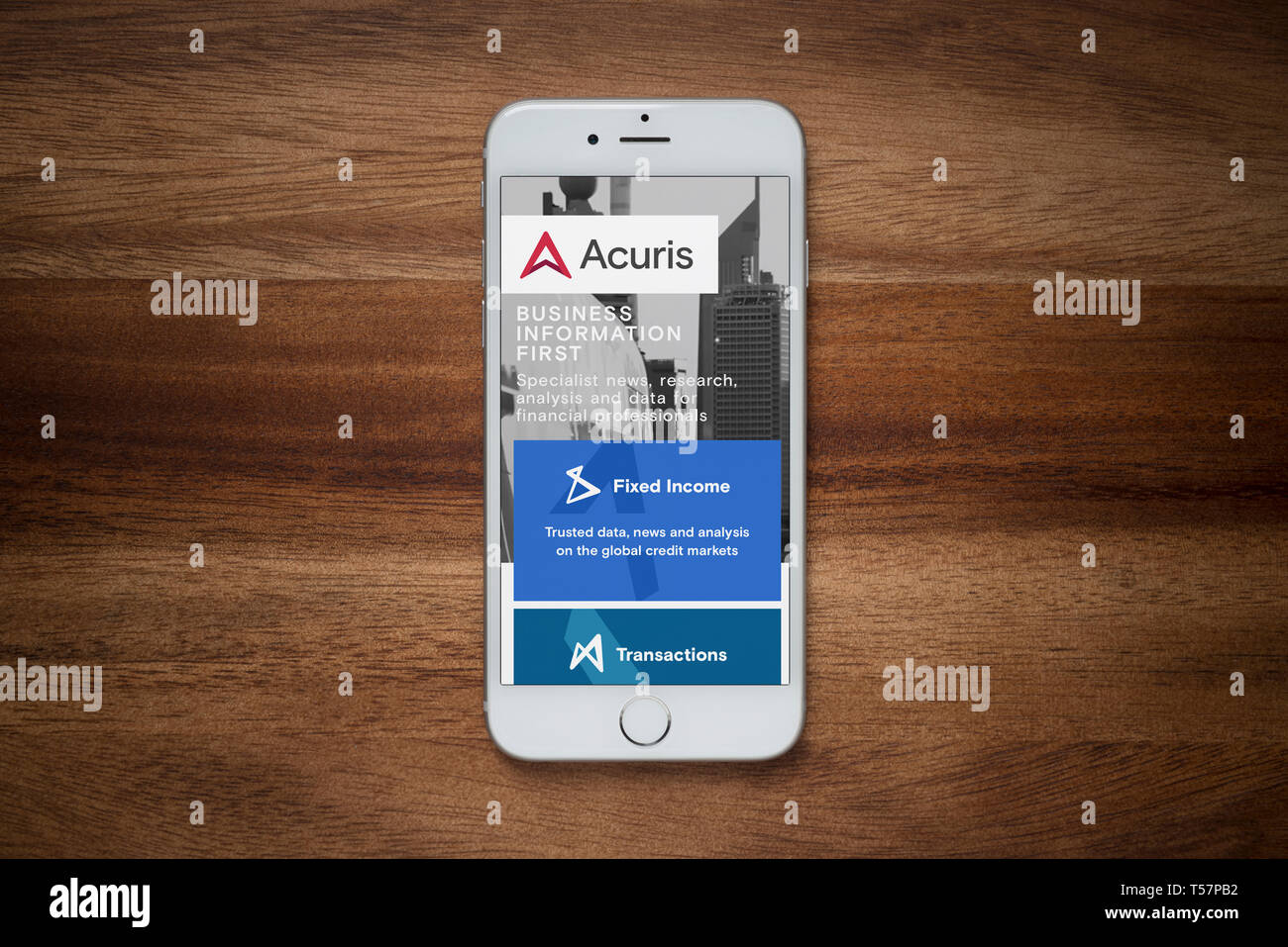 An iPhone showing the Acuris website rests on a plain wooden table ...