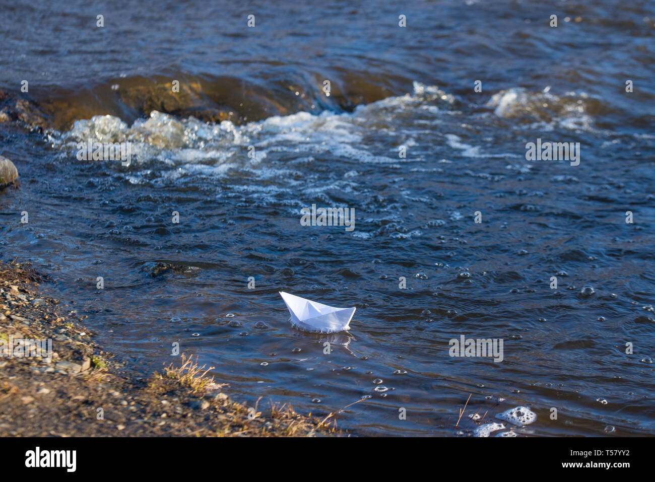 A paper boat on a turbulent stream of water struggles with the flow ...