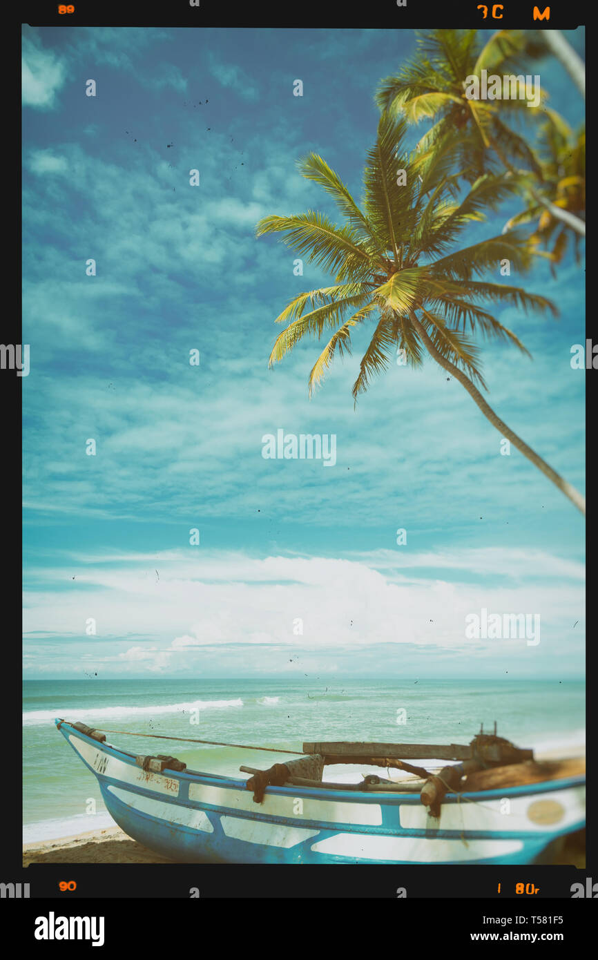 Small wooden fishing boat under palm tree on tropical beach, retro film ...