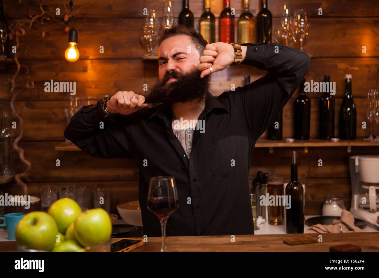 Bearded barman being funny with his beard behind the counter in vintage ...