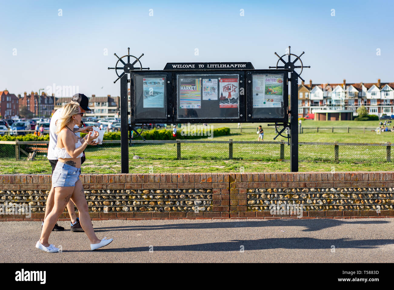 A young couple eating fast food walking along the promenade in ...