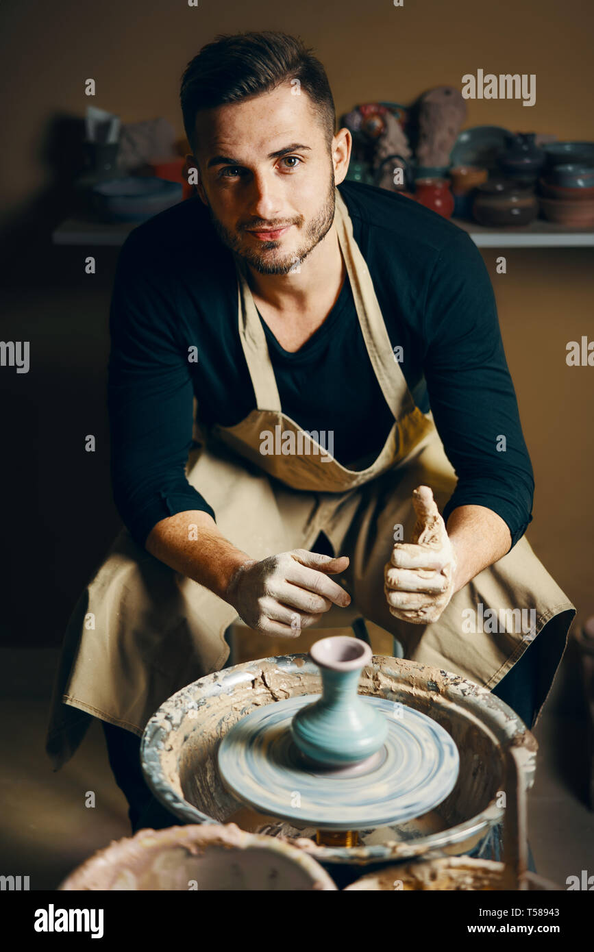 Smiling handsome man showing handmade ceramic pot at pottery workshop ...