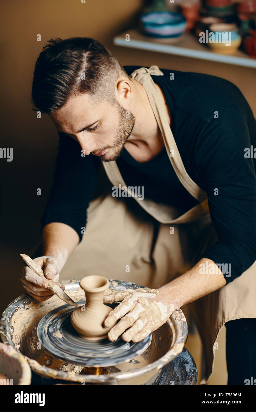 Man potter working on potters wheel making ceramic pot from clay in ...