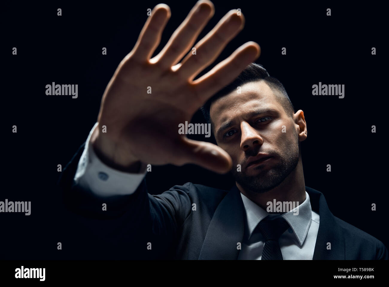 Handsome man in suit showing stop sign isolated on dark background ...