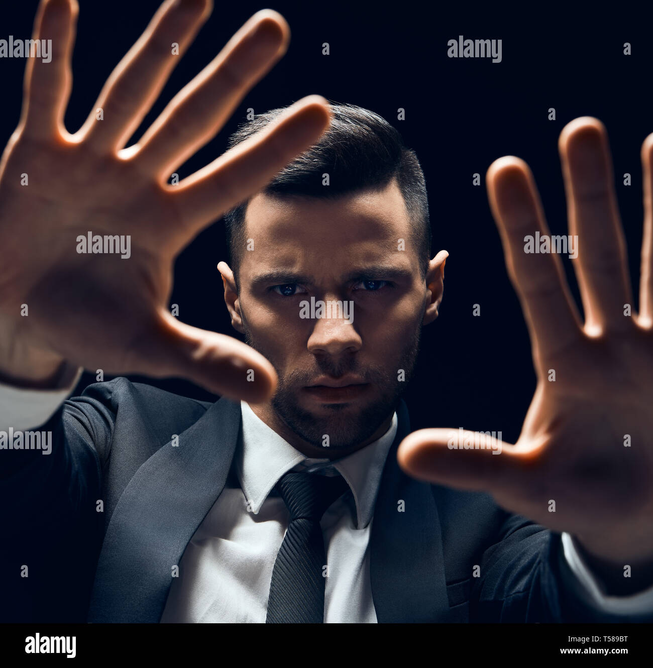 Handsome man in suit showing stop sign isolated on dark background ...