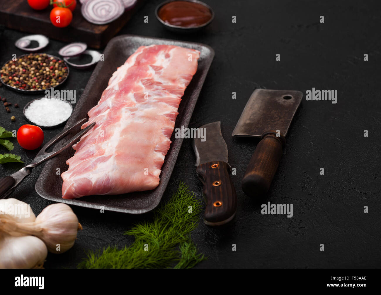 Plastic tray with raw pork ribs and vintage knife and fork on black ...