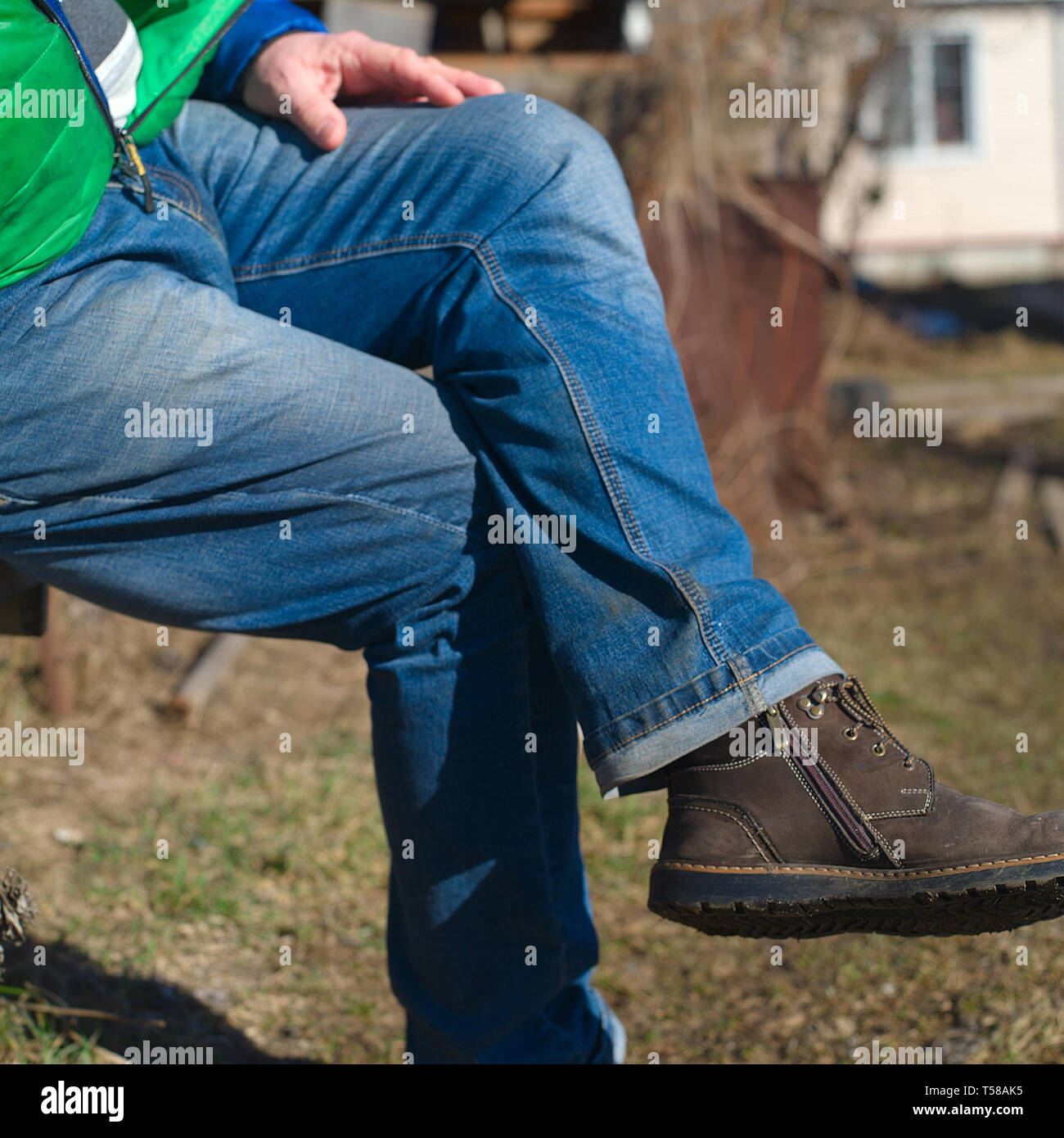 A man in blue jeans and jacket sitting outdoor, close-up side shot ...