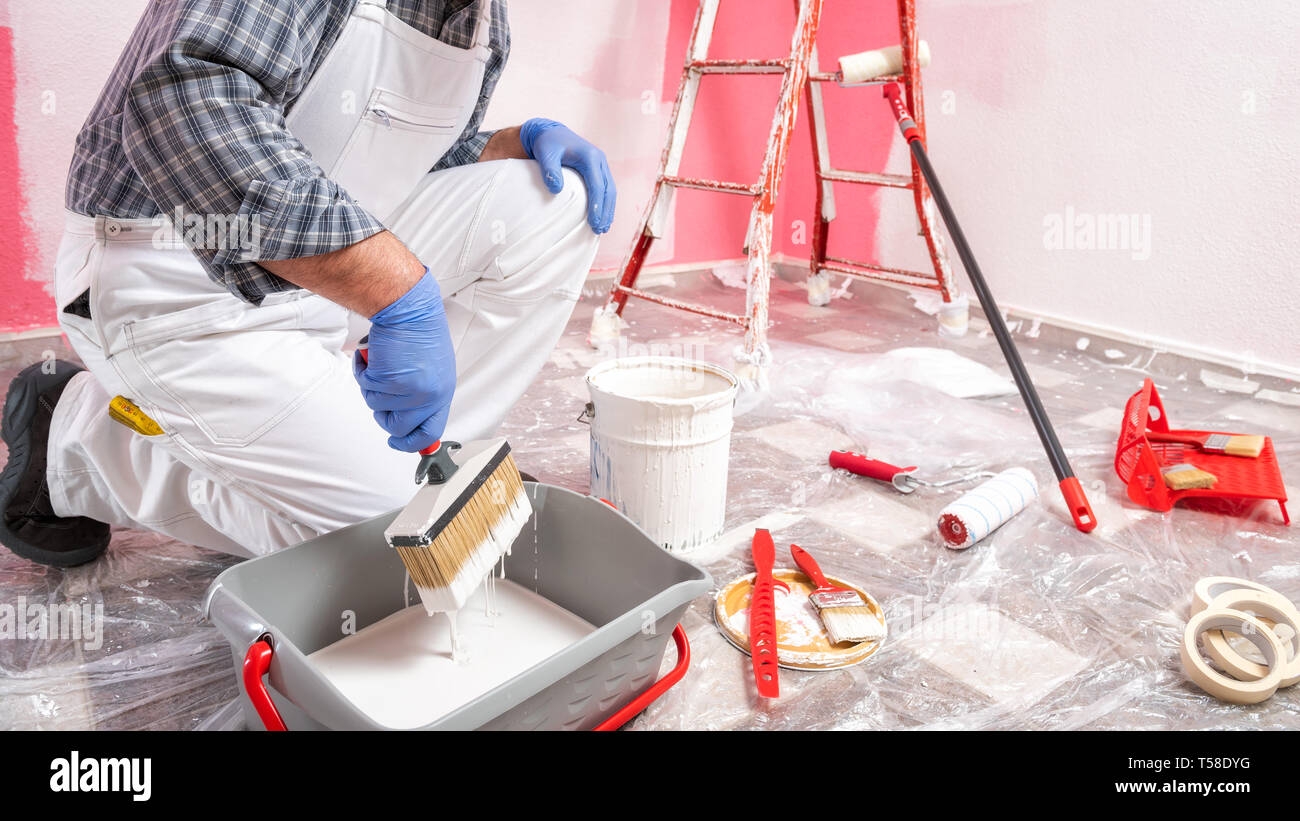 Caucasian house painter worker in white overalls, prepares the white ...