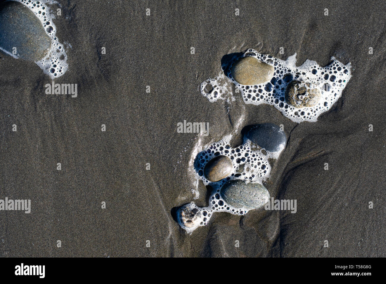 Rocks in foamy sand during low tide Stock Photo - Alamy