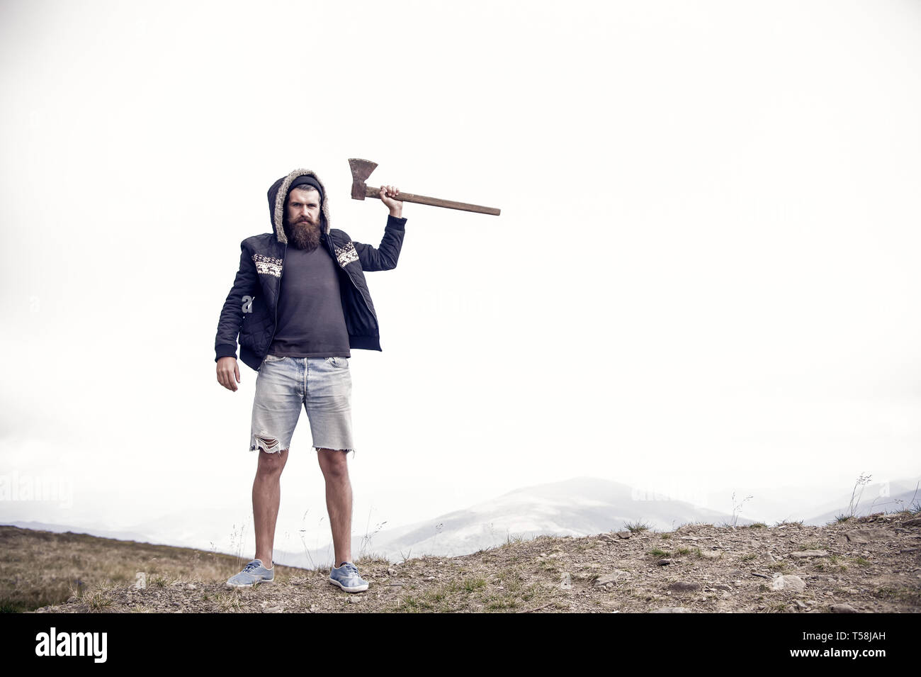 Man brutal bearded hipster with axe stand on mountain top on white sky ...