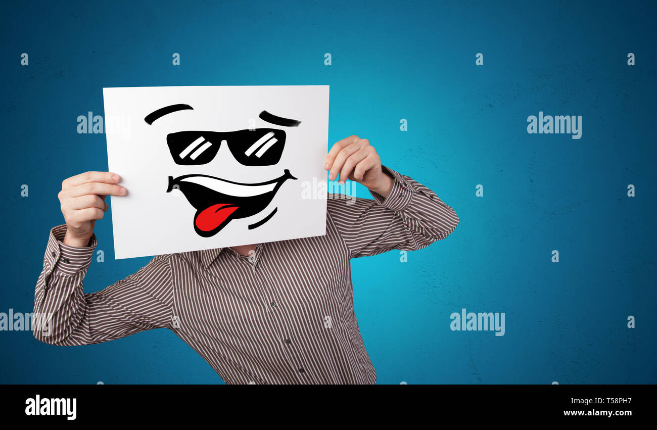 Casual person holding a paper with cool emoticon in front of his face ...