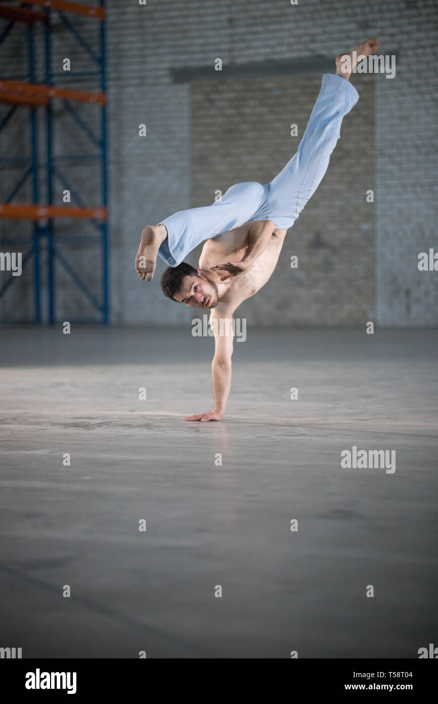 An athletic man on capoeira training. Standing on one hand and legs in ...