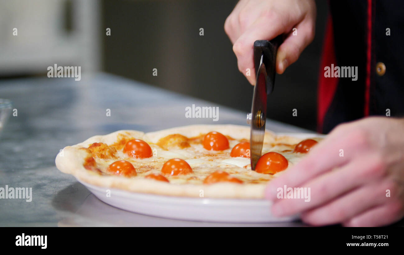 Restaurant kitchen. A chef cutting the pizza on pieces Stock Photo - Alamy
