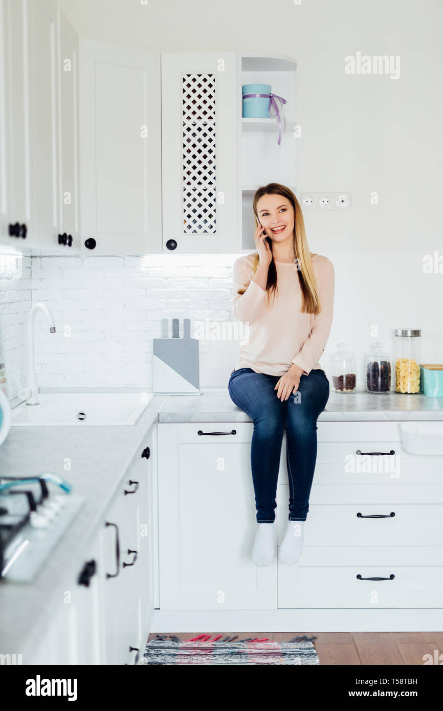 Young woman sitting a table in the kitchen Stock Photo - Alamy