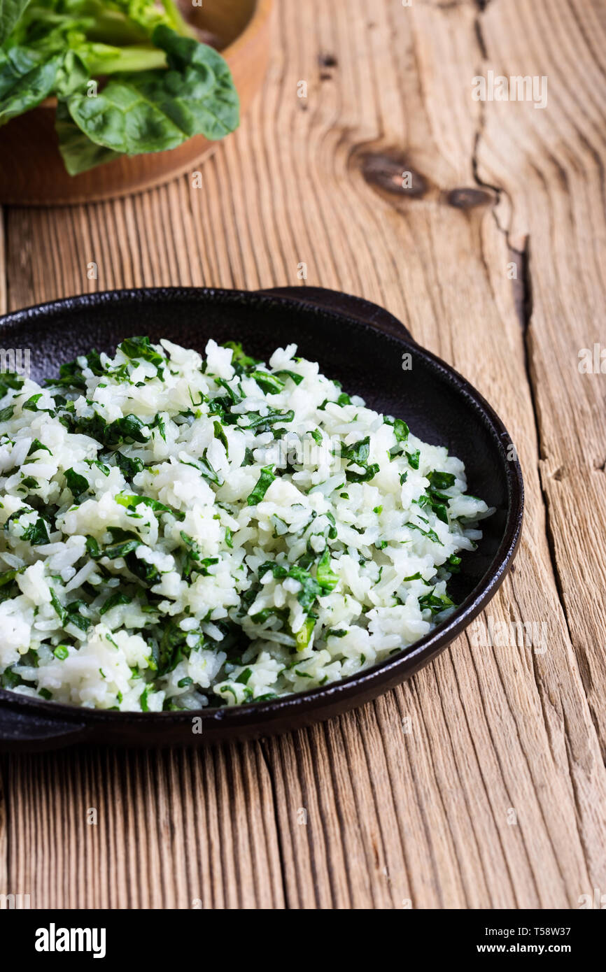 White rice with spinach served in cast iron skillet on rustic wooden ...