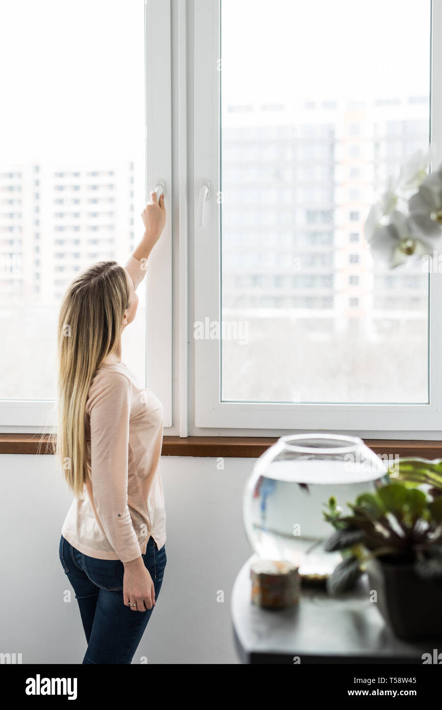 Back view of woman looking outdoors through a window and opening window ...