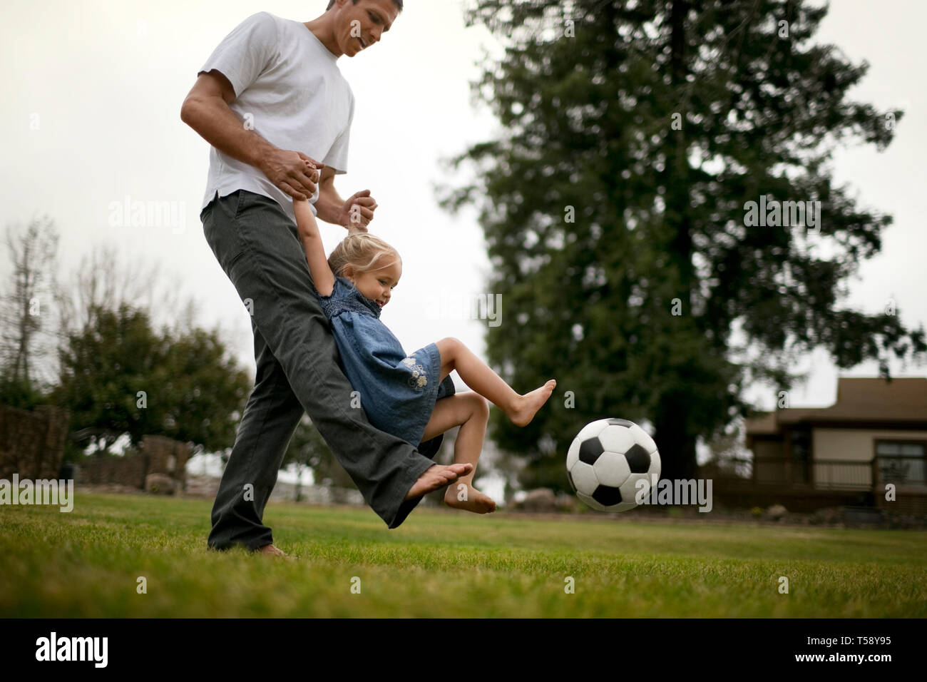 Smiling father teaches his little girl how to kick a soccer ball on the ...
