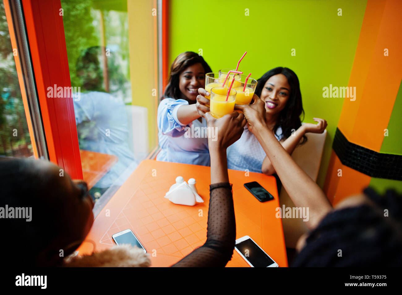 Four young african girls cheers with orange juices while sitting in ...