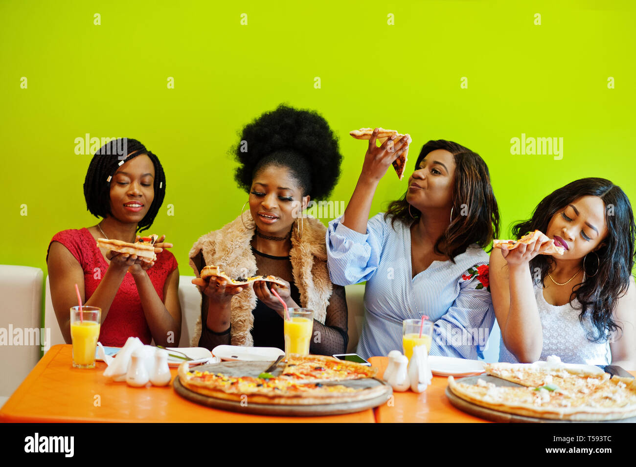 Four young african girls in bright colored restaurant eating pizza ...