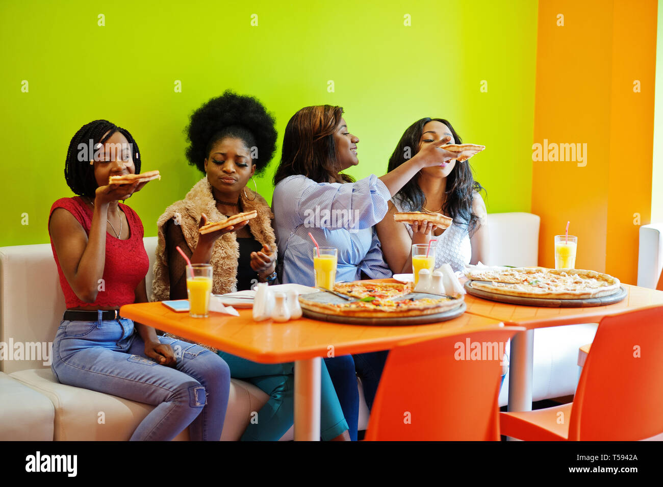 Four young african girls in bright colored restaurant eating pizza ...