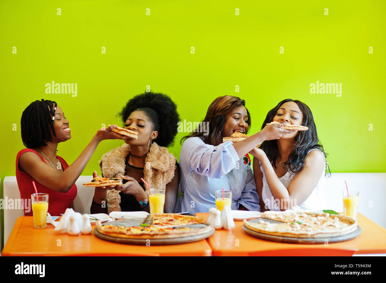 Four young african girls in bright colored restaurant eating pizza ...