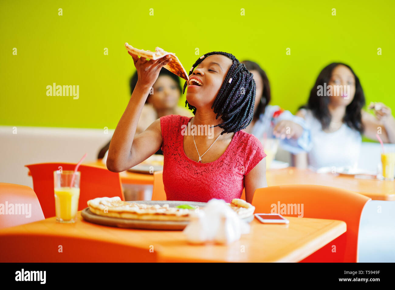 African woman with pizza sitting at restaurant against dark skinned ...