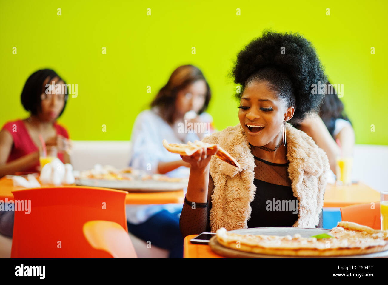 African woman with pizza sitting at restaurant against dark skinned ...