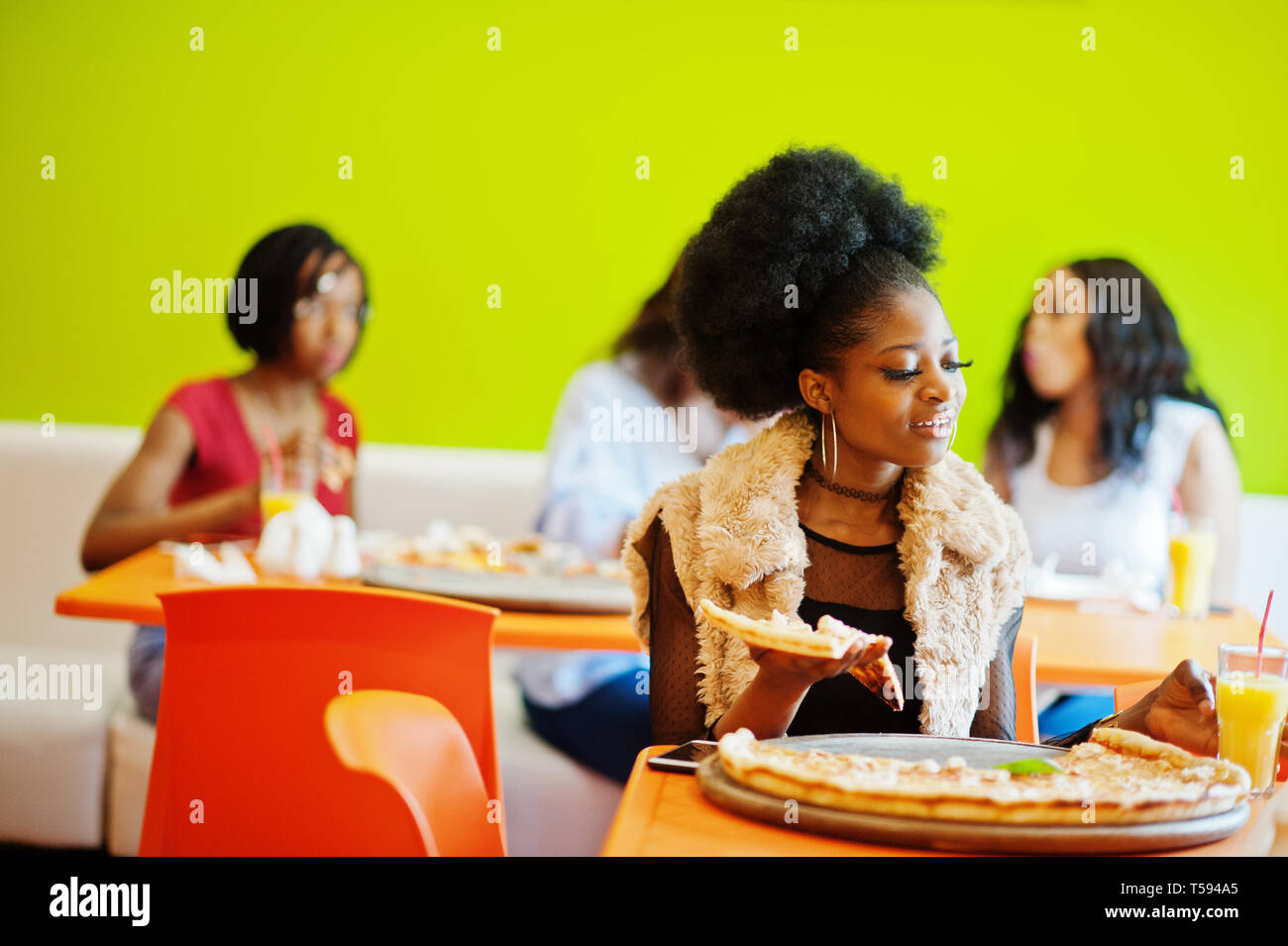 African woman with pizza sitting at restaurant against dark skinned ...