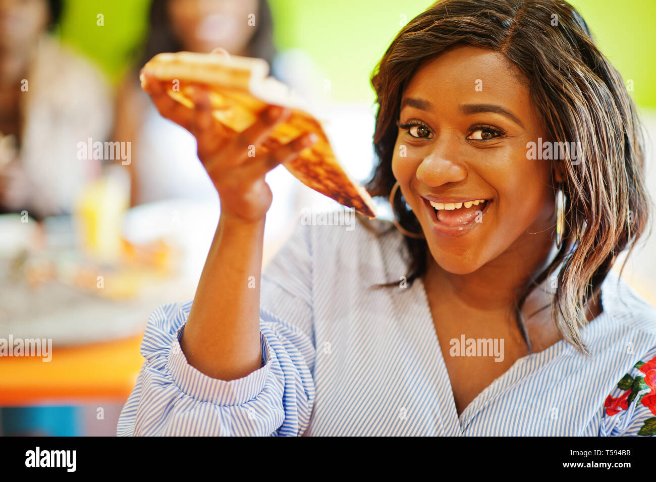 African woman with pizza sitting at restaurant against dark skinned ...