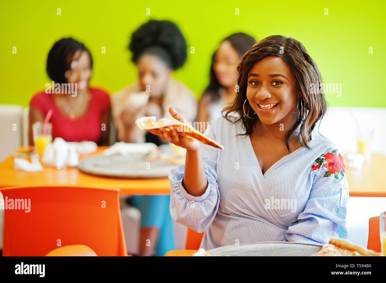 African woman with pizza sitting at restaurant against dark skinned ...