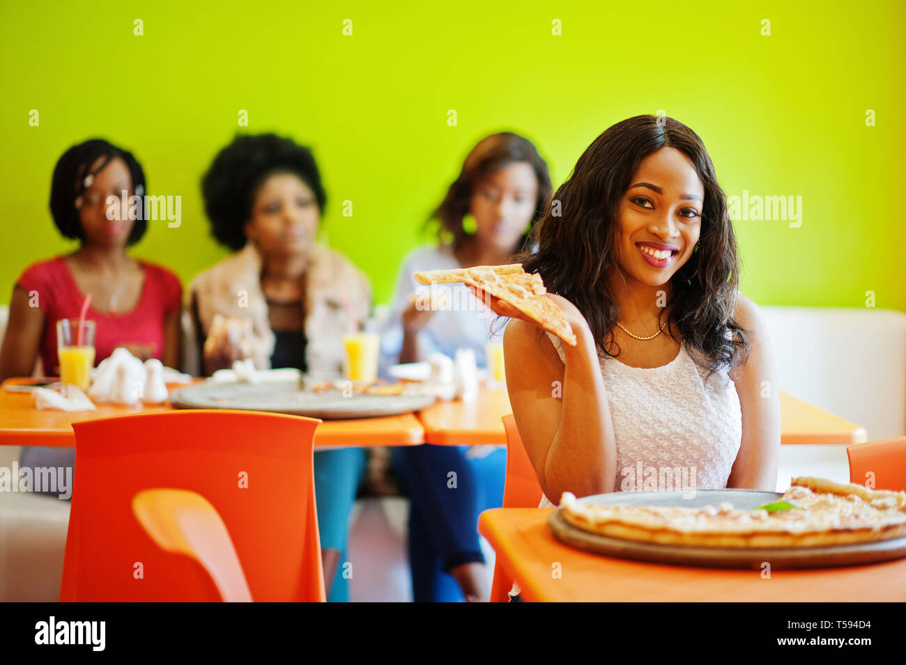 African woman with pizza sitting at restaurant against dark skinned ...