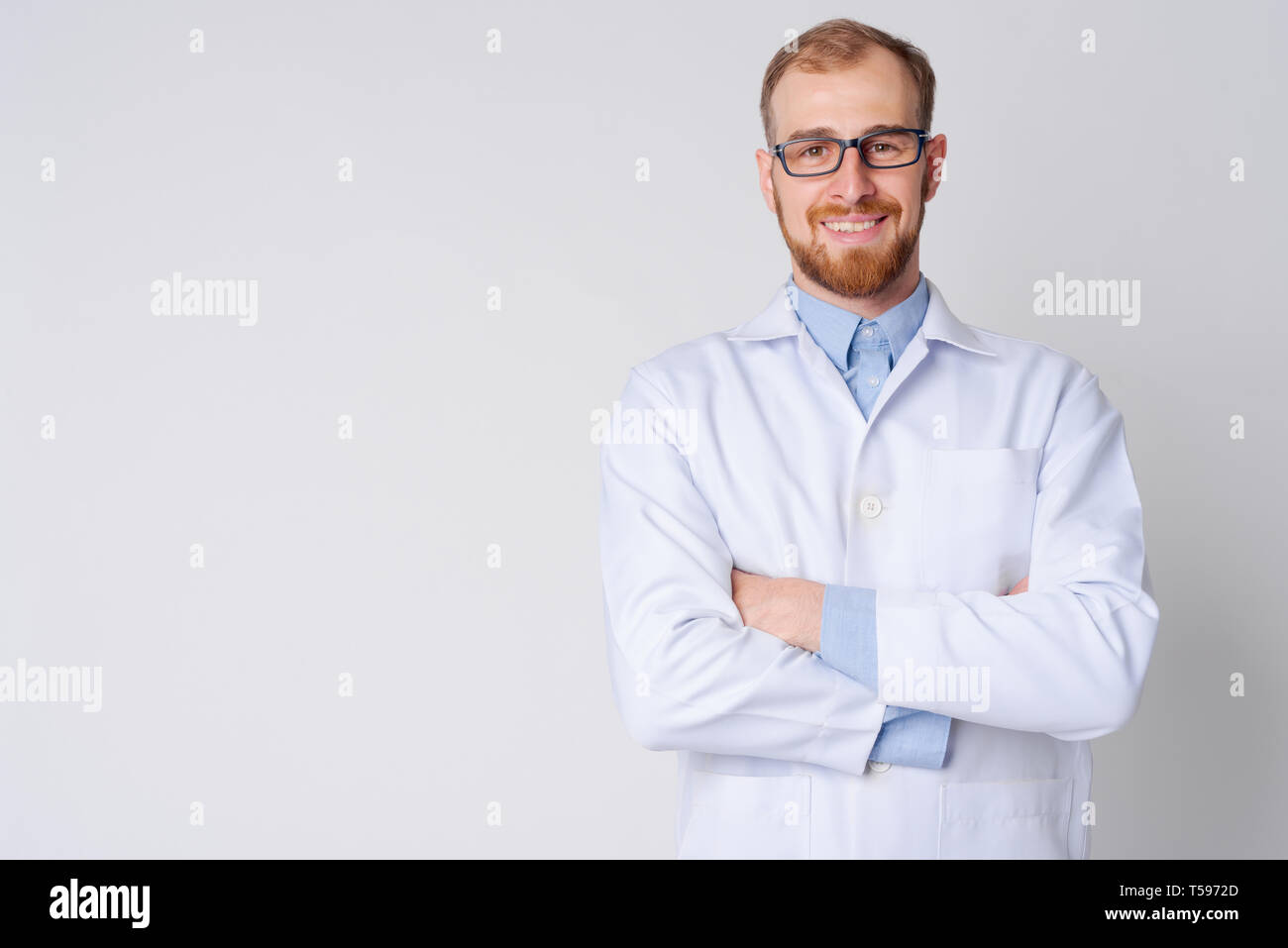 Portrait of happy young bearded man doctor wearing eyeglasses with arms ...