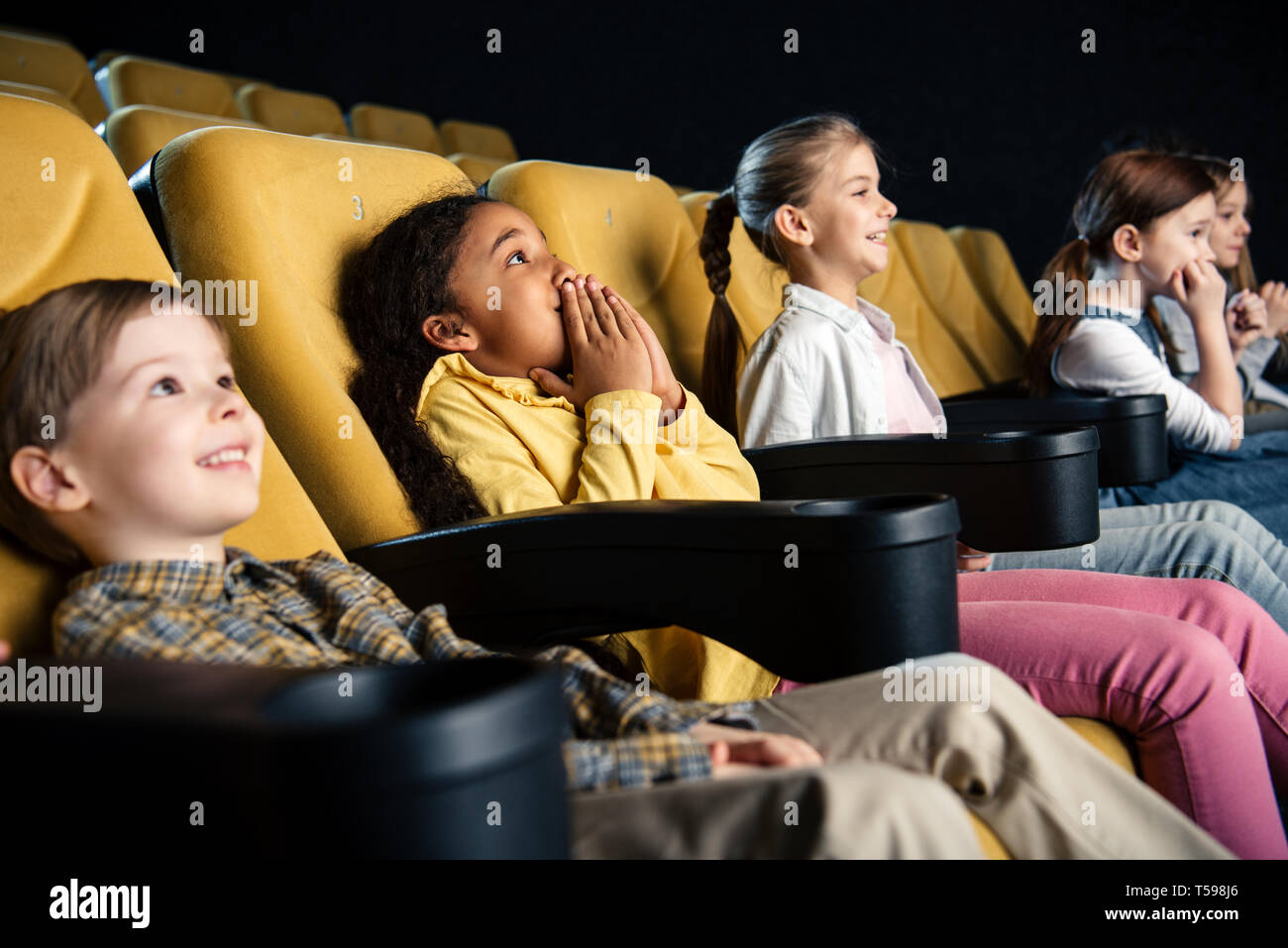 smiling multicultural friends sitting in cinema and watching movie ...