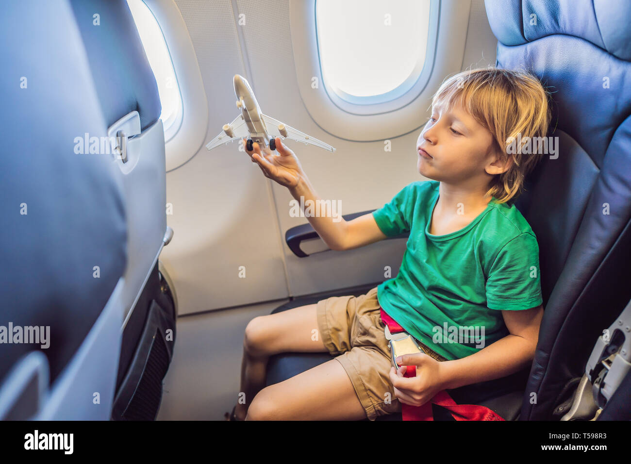 Little boy play with toy plane in the commercial jet airplane flying on ...