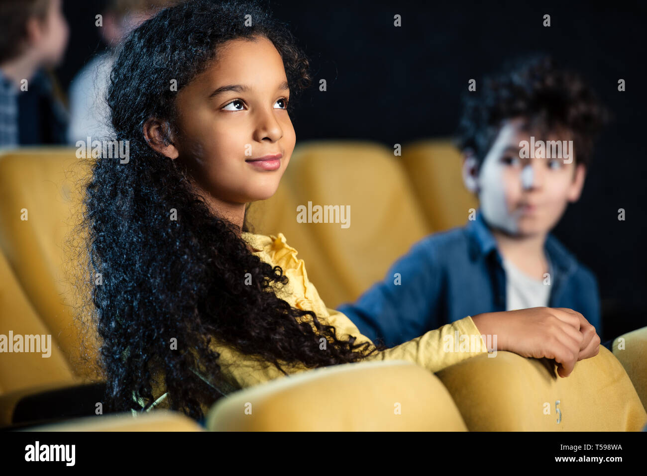 selective focus of two multicultural children sitting in cinema and ...